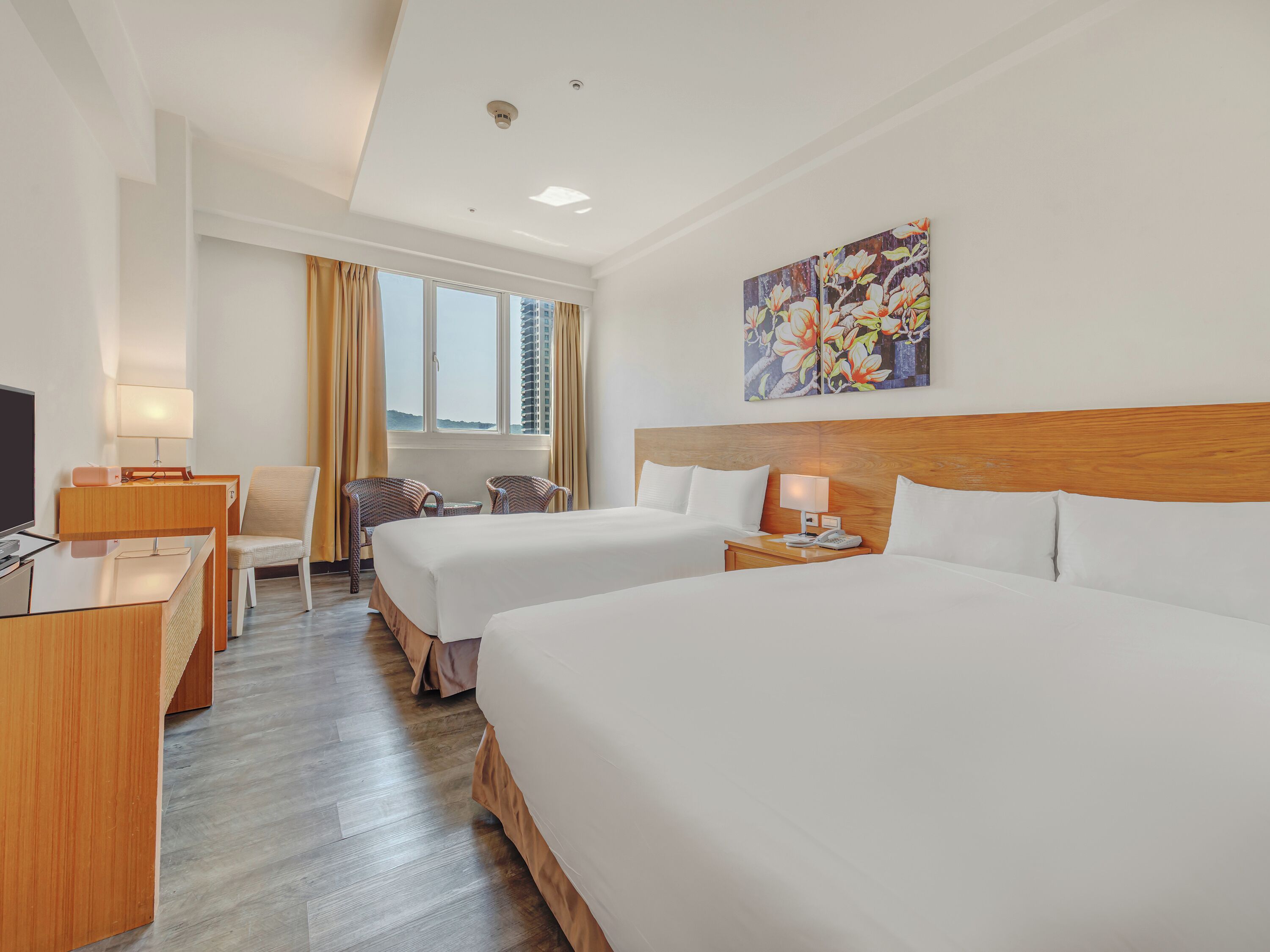 Quarto de hotel com duas camas, uma escrivaninha, televisão e janela com cortinas.
