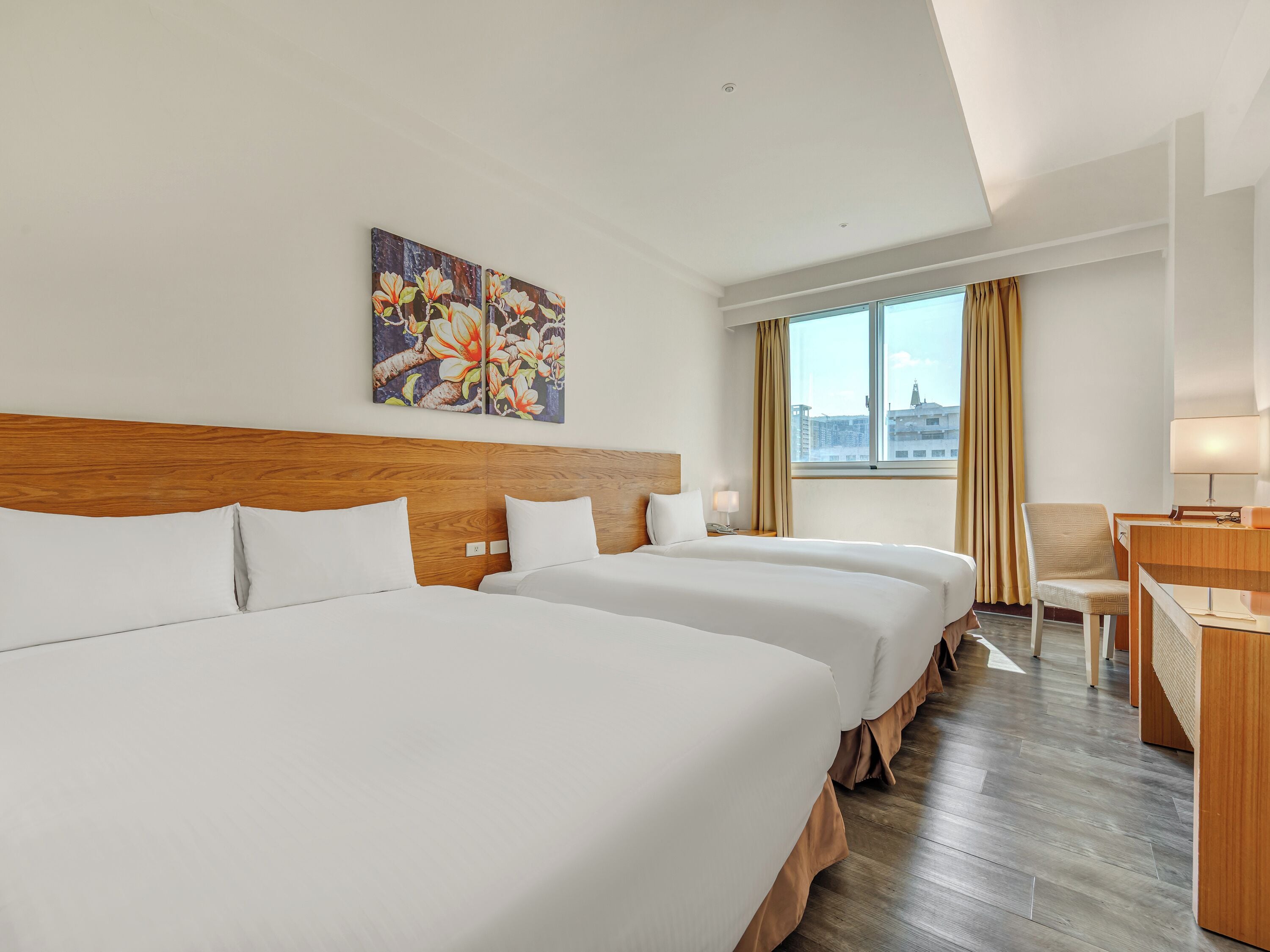 Quarto de hotel com duas camas, uma mesa, uma cadeira, uma janela com vista e um quadro na parede.