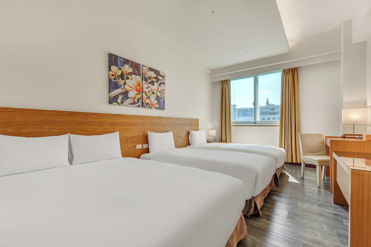 Quarto de hotel com duas camas, uma mesa, uma cadeira, uma janela com vista e um quadro na parede.