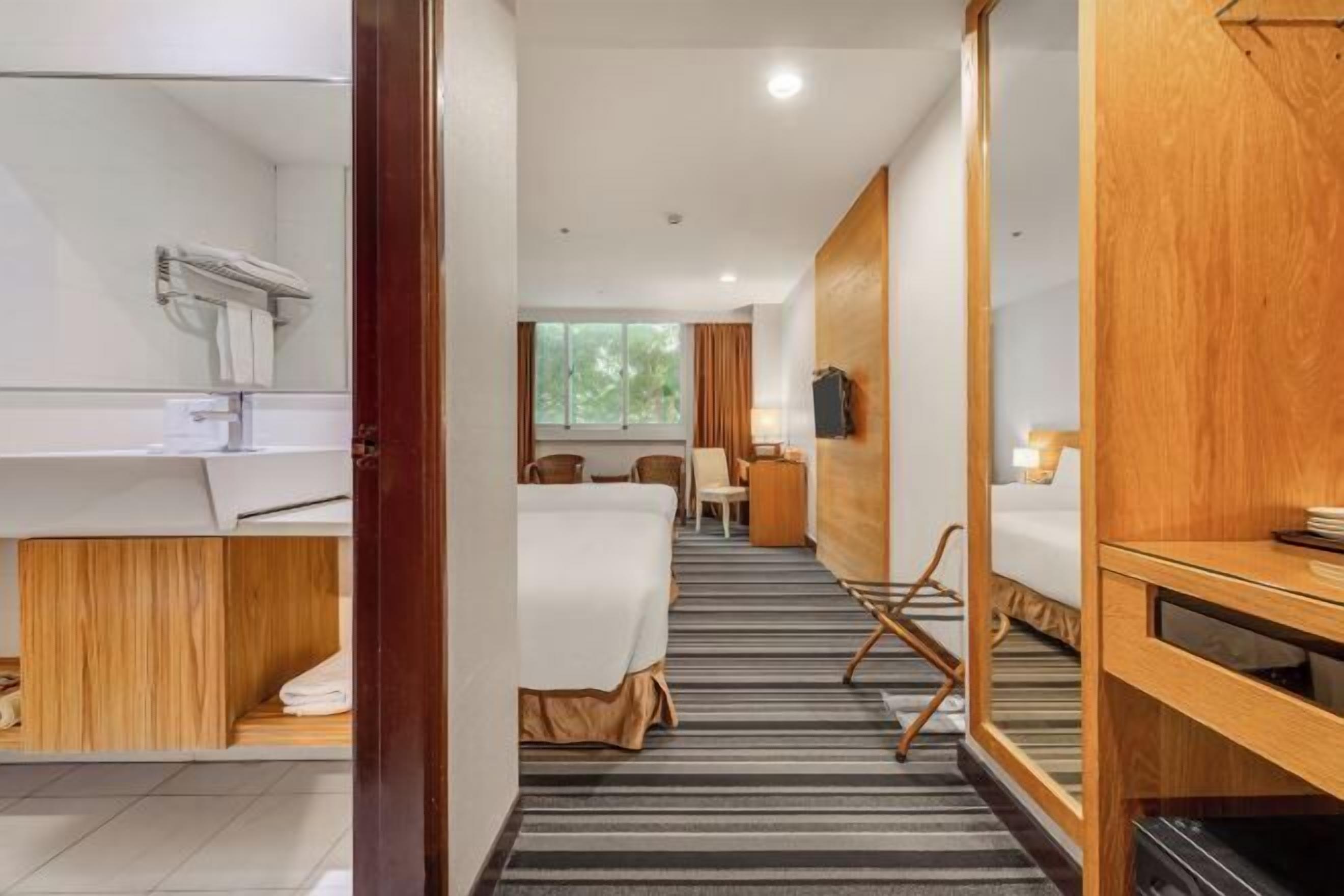 Quarto de hotel com cama, secretária, cadeira, espelho e janela.
