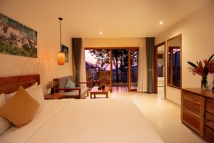 Quarto de hotel espaçoso com uma cama grande, uma escrivaninha de madeira, um sofá e uma varanda com vista para o pôr do sol.