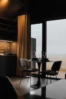 Uma área de jantar moderna com vista para o mar, com uma mesa posta com taças de vinho e uma vela.