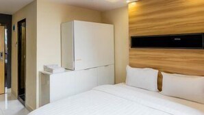 Quarto de hotel moderno com uma cama grande, cabeceira de madeira e televisão integrada.