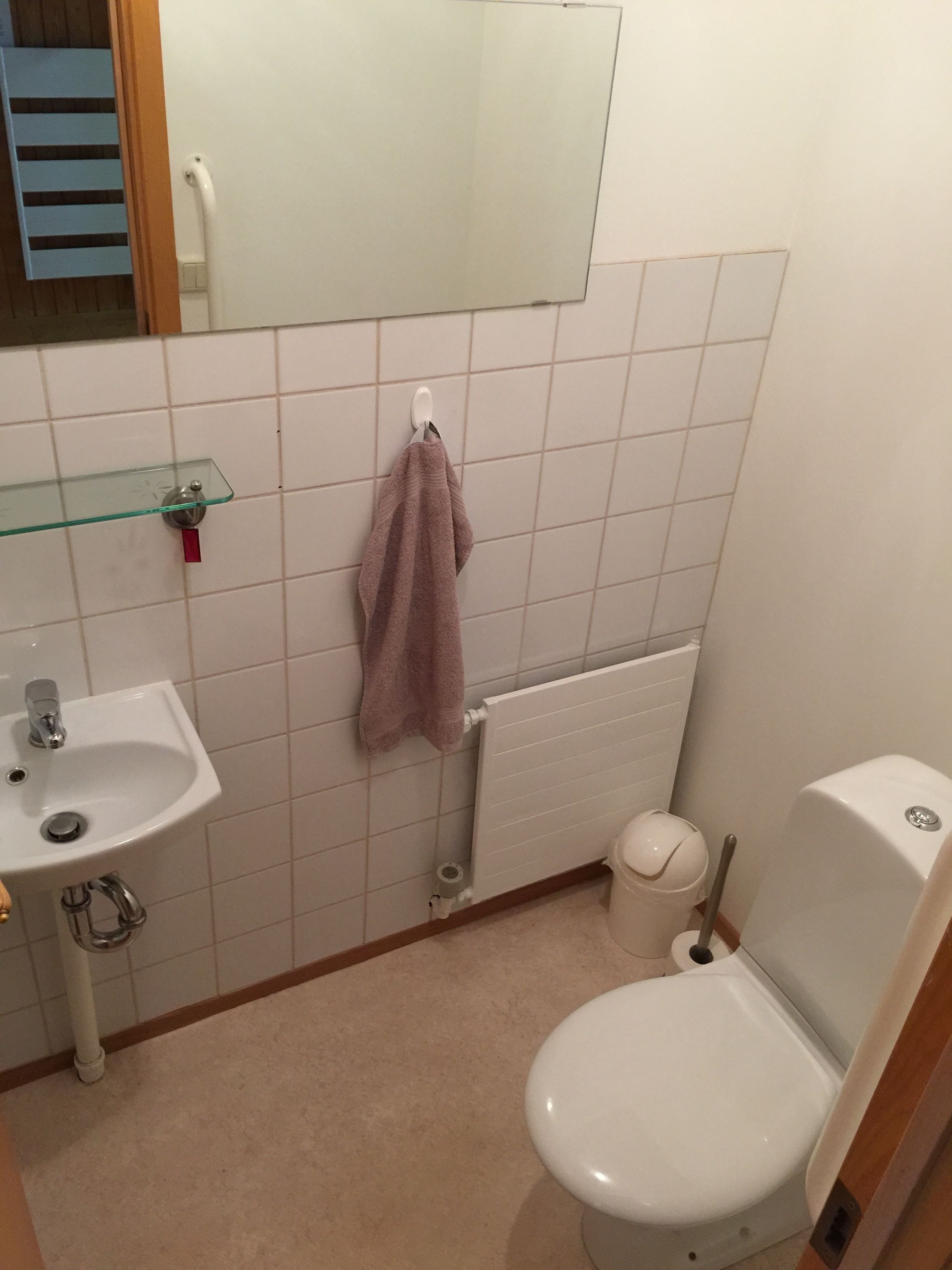 Casa de banho com lavatório branco, sanita, prateleira de vidro e toalha pendurada na parede.
