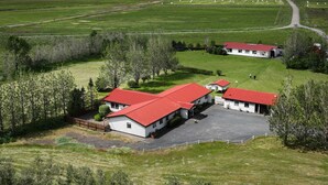 Uma propriedade rural com vários edifícios, zona de estacionamento cercada e extensos campos verdes.