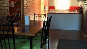 Uma área de refeições com parede de tijolos, teto de madeira e uma cozinha ao fundo.