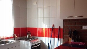 Uma cozinha compacta com azulejos brancos e vermelhos, fogão a gás, forno pequeno e geladeira.