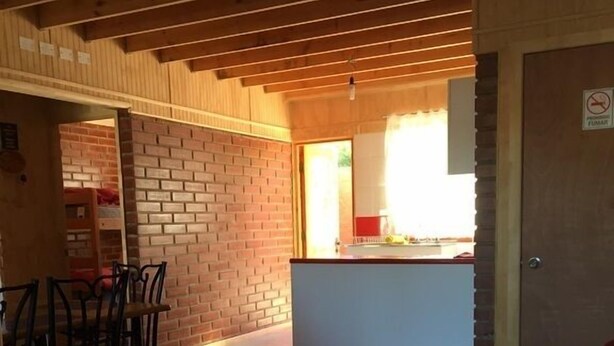 Uma sala de estar aconchegante com sofá, uma mesa de jantar com cadeiras e uma cozinha ao fundo.