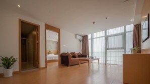 Quarto de hotel moderno com piso de madeira, um sofá, uma cama e janelas amplas.