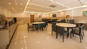 Ampla área de refeições de hotel, com várias mesas redondas e cadeiras, um buffet e um design moderno e elegante.