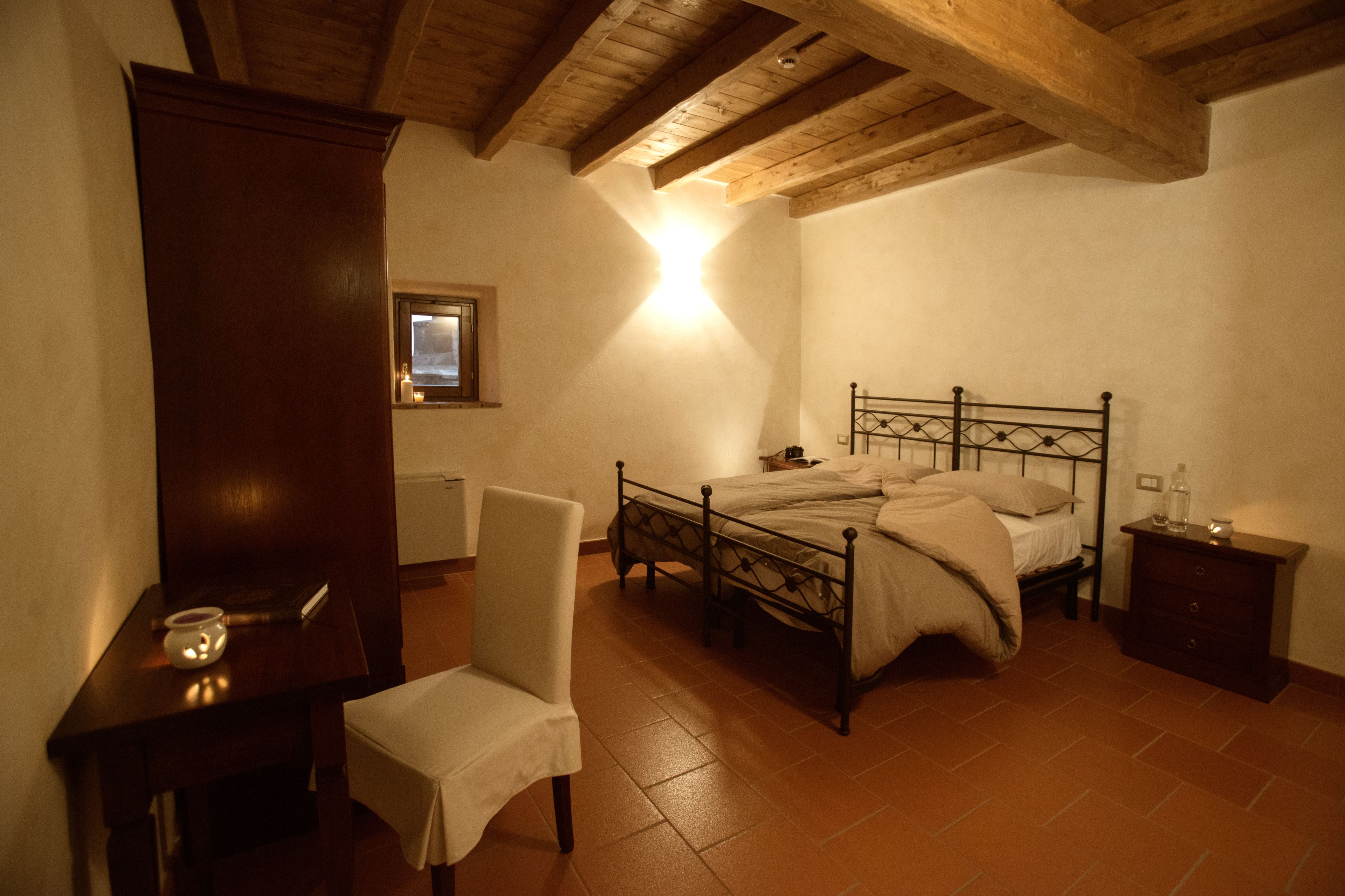 Um quarto com cama de madeira, mesa de cabeceira, uma cadeira e um criado-mudo.