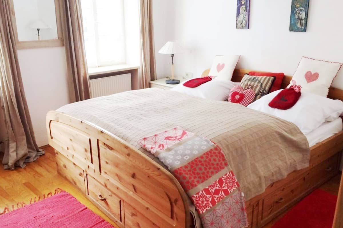 Uma cama de madeira com colcha, almofadas e mesa de cabeceira com abajur.