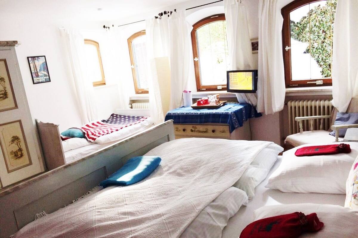 Quarto com duas camas, uma escrivaninha com computador e uma janela com cortinas.