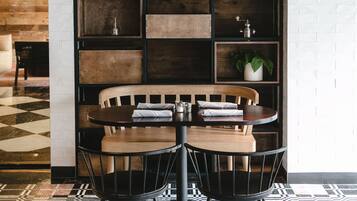 Um interior moderno com chão quadriculado em preto e branco, uma mesa de madeira com cadeiras e uma prateleira na parede com objetos decorativos.