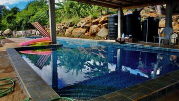 Piscina com borda azulejada, rodeada por pedras e vegetação.