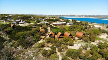 Vista aérea de um resort com várias cabanas no estilo de casas na árvore, rodeadas por vegetação densa, uma praia arenosa e um mar azul cristalino ao fundo.