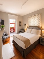 Quarto com cama grande, luminárias laterais, TV, cadeira e vista para o exterior.