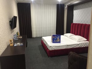 Quarto de hotel com uma cama, uma secretária e uma TV fixada na parede.