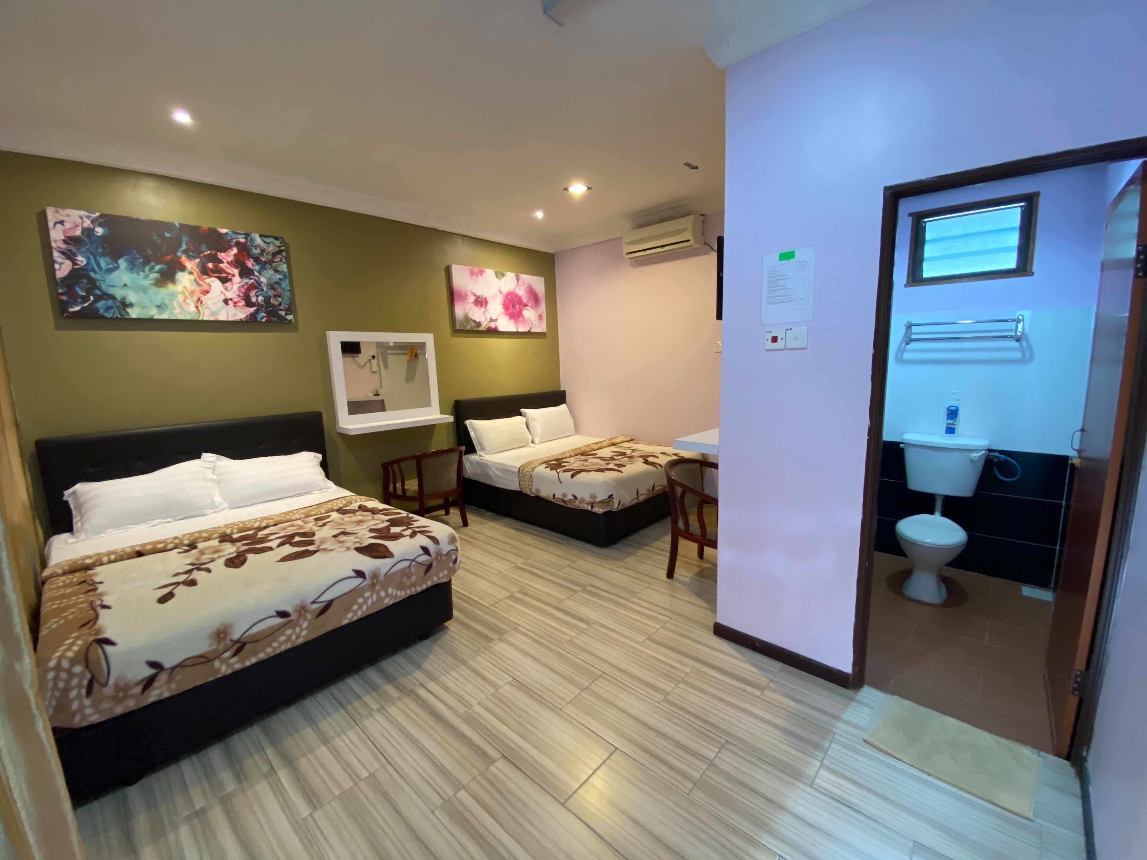 Quarto de hotel com duas camas, uma mesa pequena, um espelho e banheiro com vaso sanitário e pia.