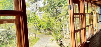 Janela de madeira com vista para um caminho de pedra que serpenteia por um jardim exuberante.