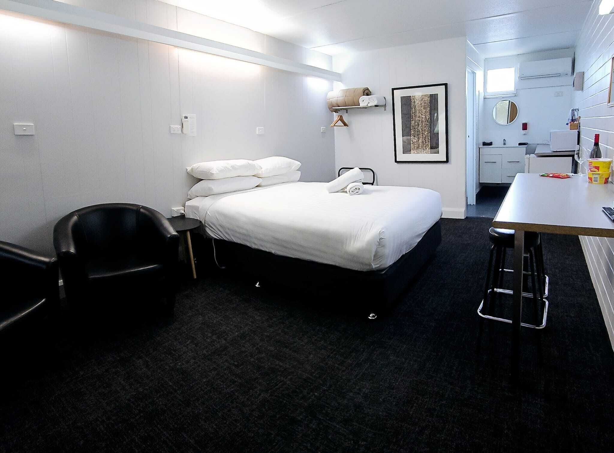 Quarto de hotel com cama, escrivaninha, cadeira, mesinha, espelho e um quadro na parede.
