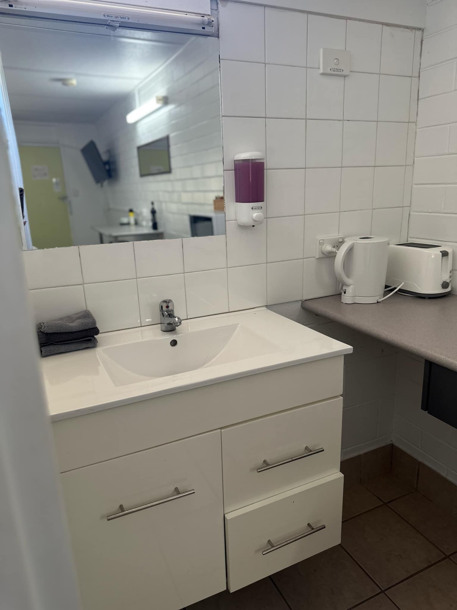 Casa de banho moderna com lavatório branco, espelho e máquina de café.