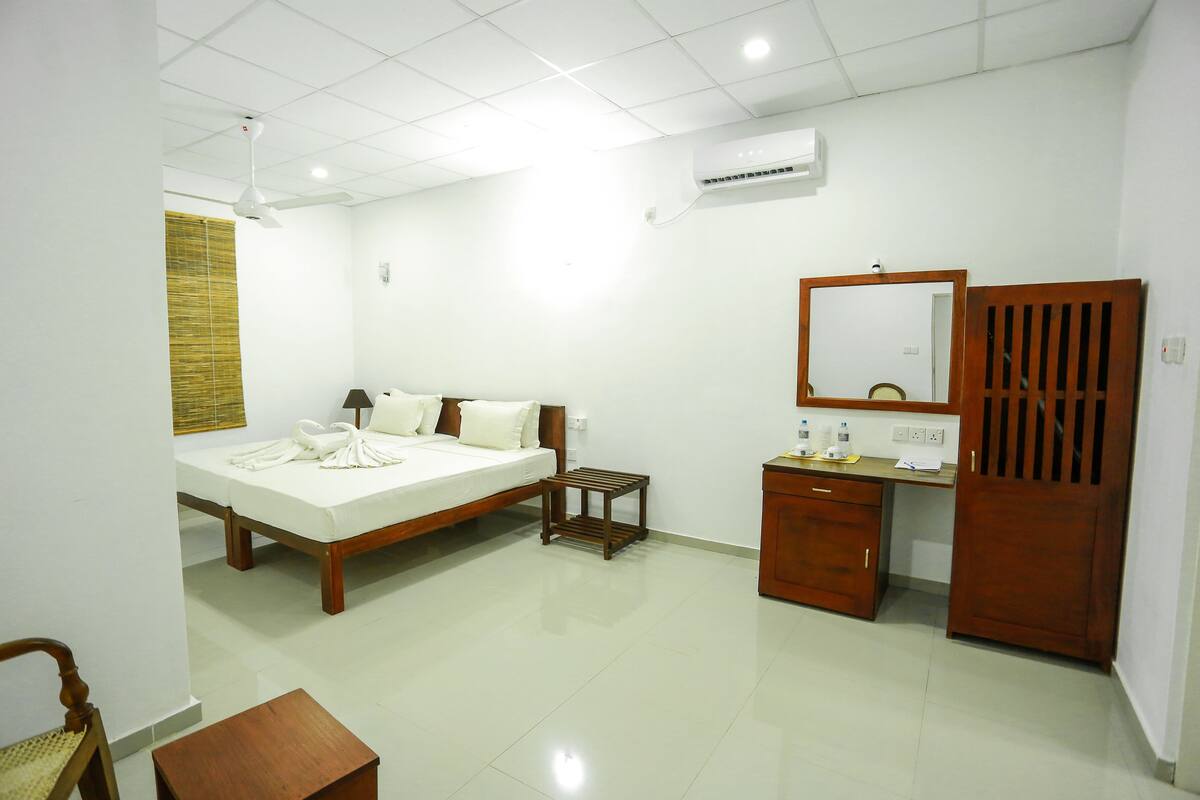 Quarto de hotel com cama, mesa de cabeceira, guarda-roupa de madeira e escrivaninha com espelho.