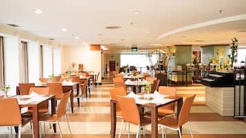 Um restaurante amplo com várias mesas e cadeiras, um balcão com uma máquina registadora e uma escadaria que leva a um andar superior.