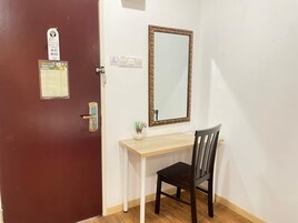 Quarto com escrivaninha de madeira, uma cadeira, um espelho e uma porta com uma placa.