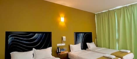 Quarto de hotel com duas camas, uma mesa de cabeceira, uma luminária e uma janela com cortinas.