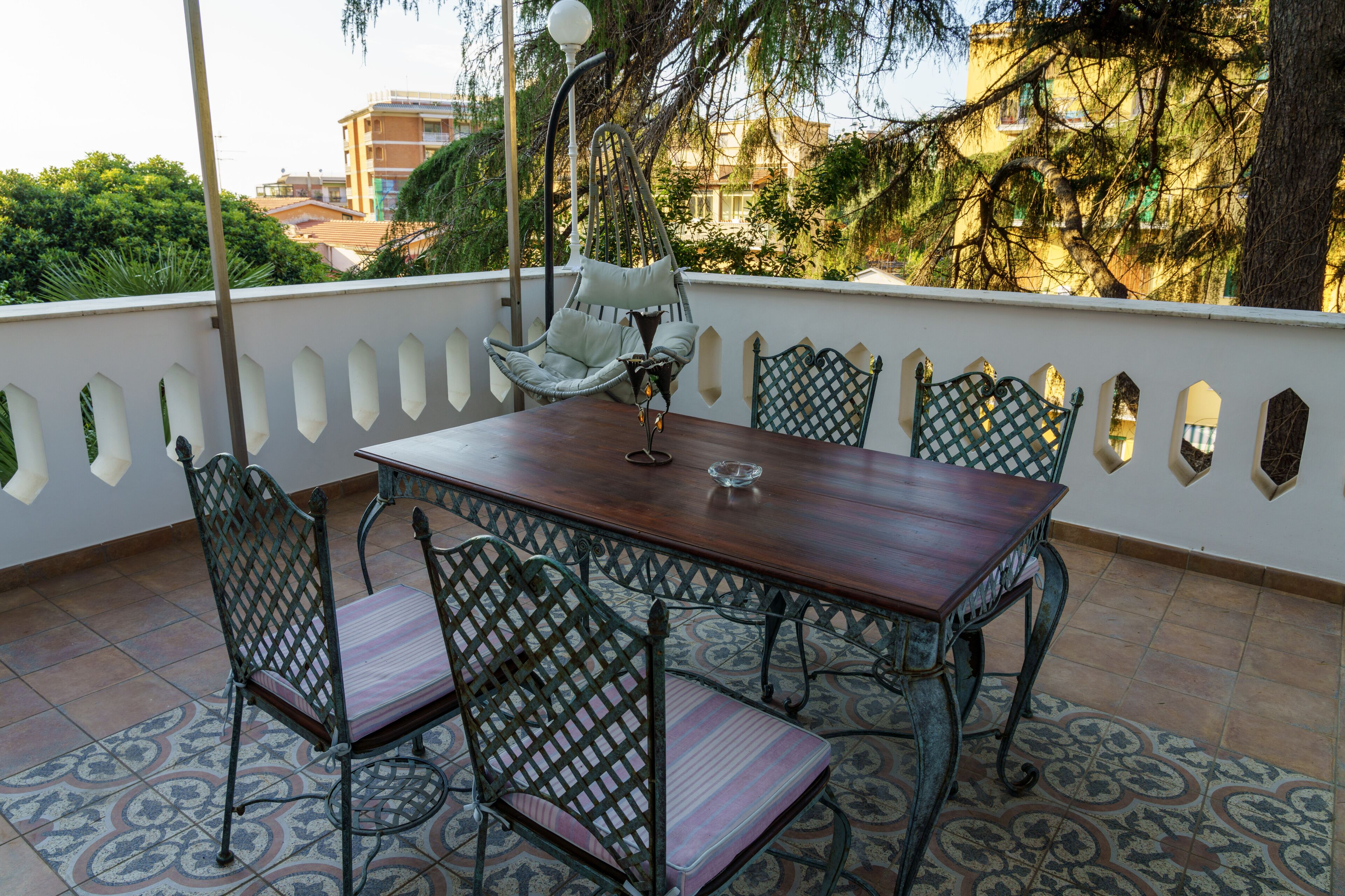 Uma varanda com uma mesa de madeira e cadeiras de metal, uma cadeira suspensa e luminárias decorativas na parede.