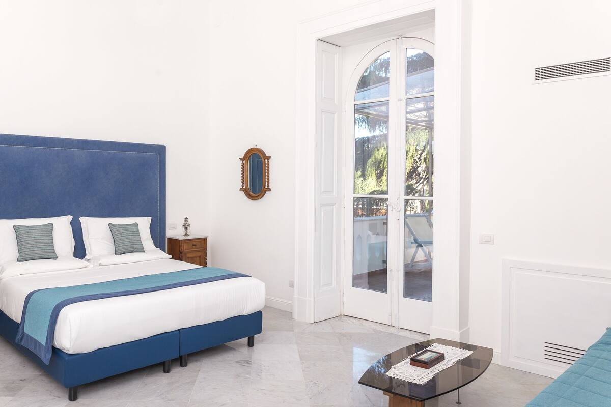 Quarto com uma cama grande, mesa de cabeceira, penteadeira e mesa de centro de vidro.