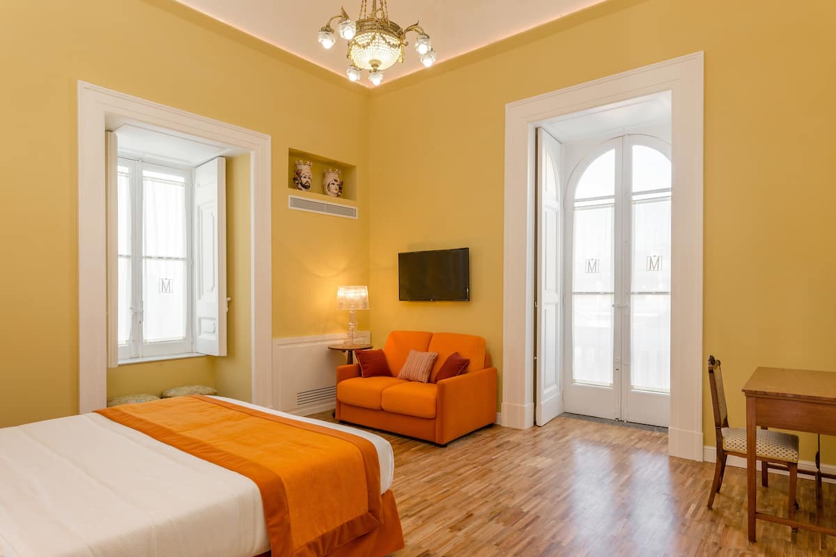 Quarto com uma cama, um sofá laranja, uma mesa de madeira e uma televisão na parede.