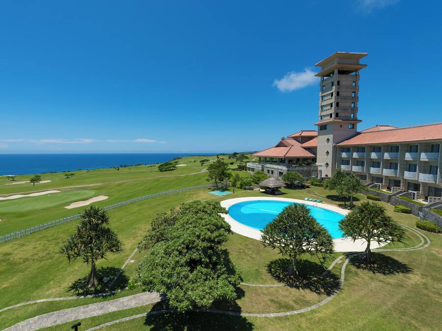 Um campo de golfe com piscina, torre e vista para o oceano.