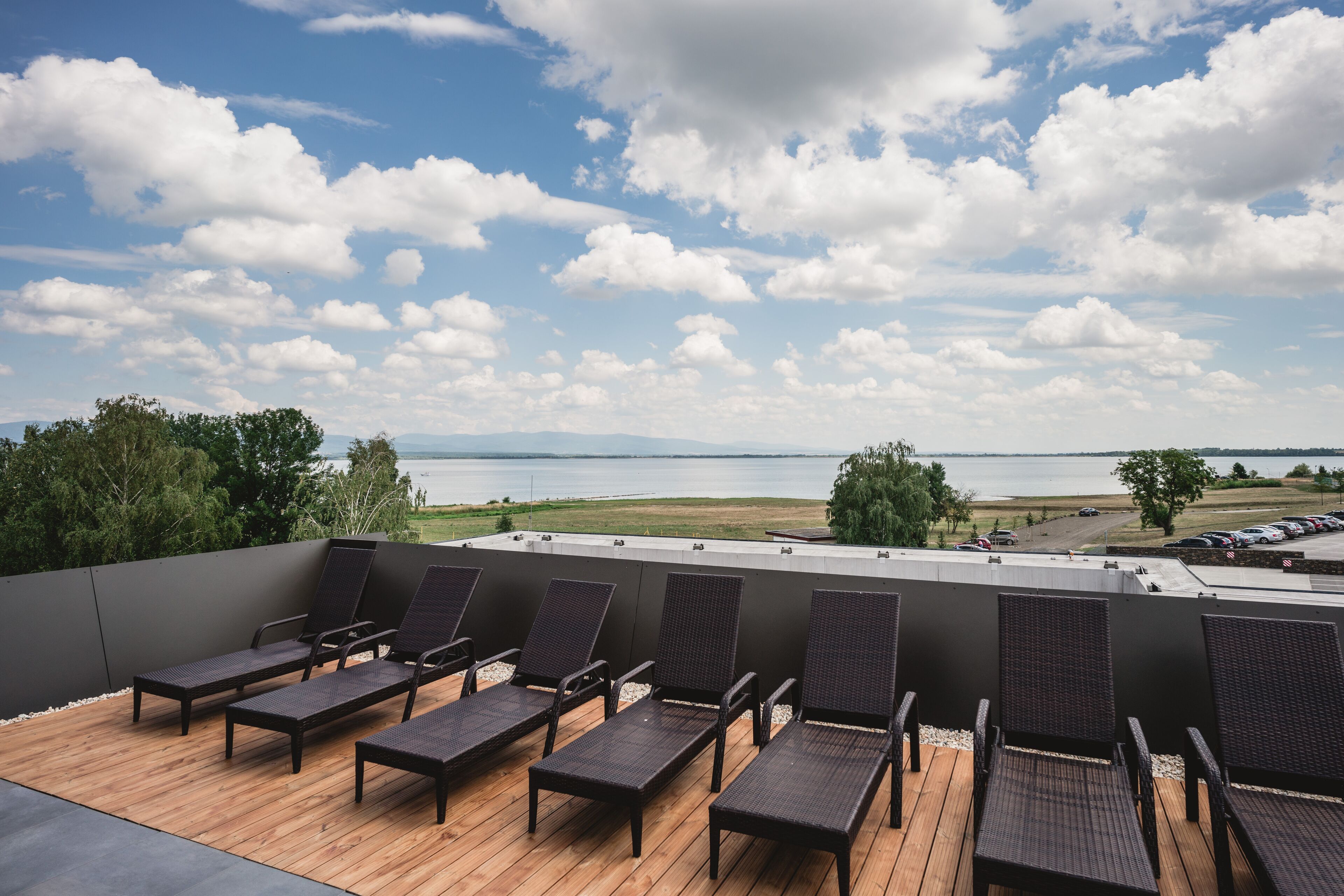 Terraço no terraço com seis poltronas de vime escura voltadas para uma vista panorâmica de um lago e montanhas.