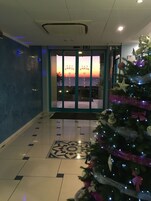 Um saguão de hotel com árvore de Natal, porta de vidro e piso estampado.