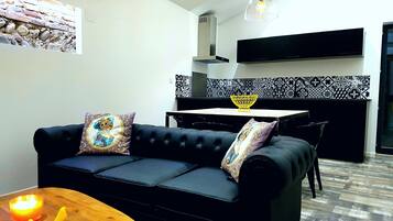 Uma sala de estar moderna com um sofá preto, uma mesa de centro de madeira e uma vela acesa.