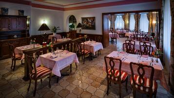 Um restaurante com chão de azulejos hexagonais, cadeiras de madeira com almofadas listradas e mesas dispostas com toalhas brancas e talheres.