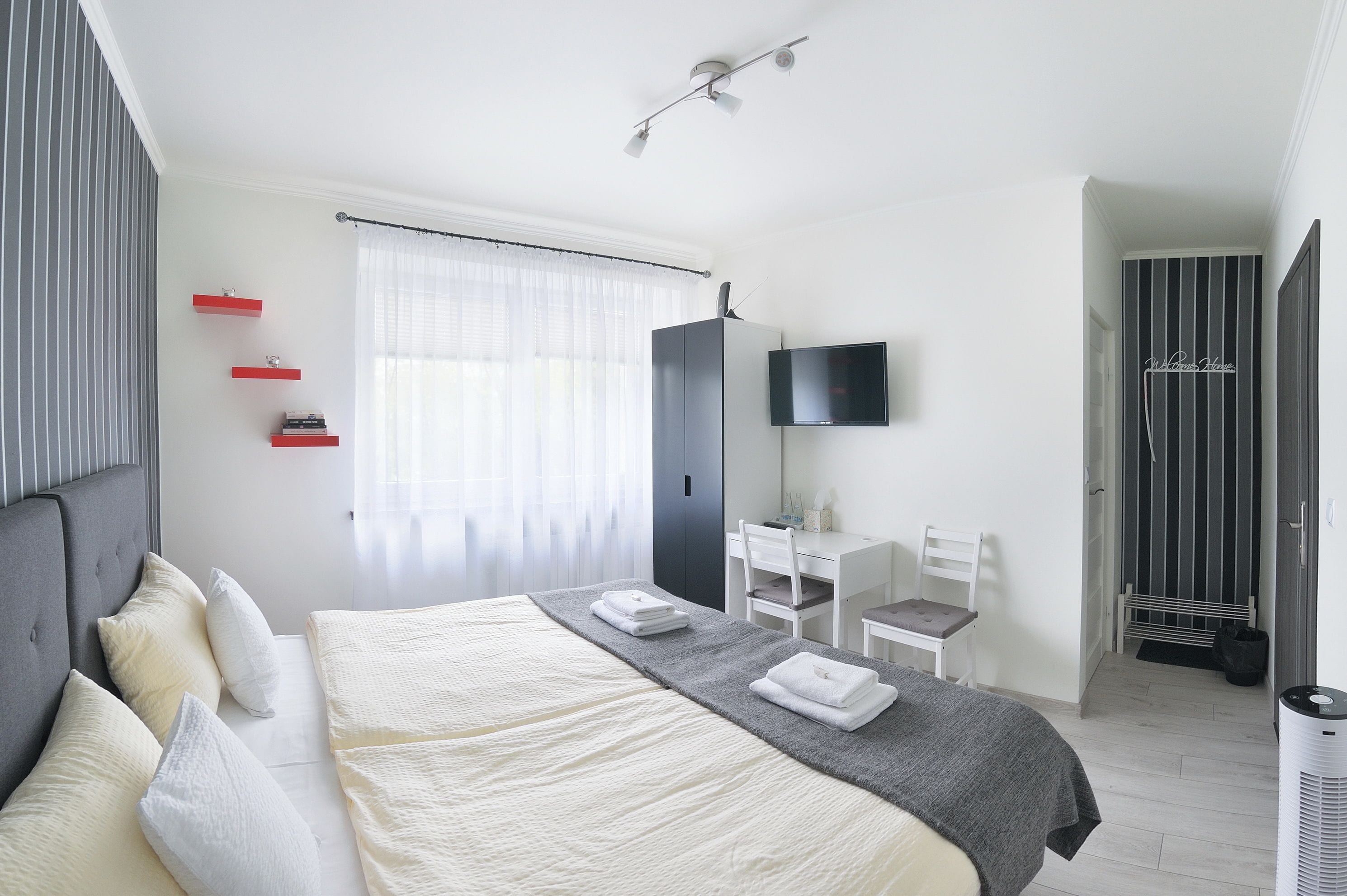Quarto moderno com uma cama grande, uma escrivaninha, uma cadeira, uma TV e um guarda-roupa.
