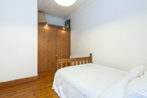 Quarto com guarda-roupa de madeira, cama com roupa de cama branca e radiador branco.