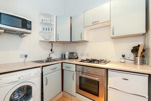 Uma cozinha compacta com máquina de lavar, forno, micro-ondas e fogão a g ás pequeno.