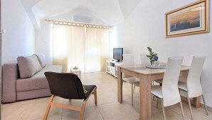 Uma sala de estar moderna com um sofá, uma mesa de jantar com cadeiras, uma televisão e um quadro na parede.
