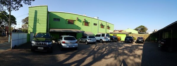 Um hotel com fachada verde, vários espaços de estacionamento e céu claro.