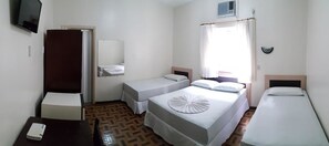 Quarto de hotel com duas camas de solteiro, uma mesa pequena, uma cadeira, televisão, espelho, janela com cortinas e ar condicionado fixado na parede.