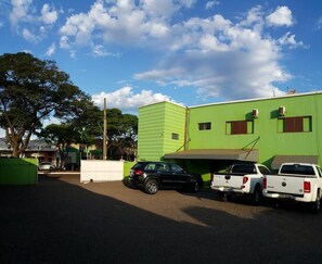 Uma área de estacionamento com dois carros estacionados em frente a um edifício verde com telhado plano e uma pequena cobertura.