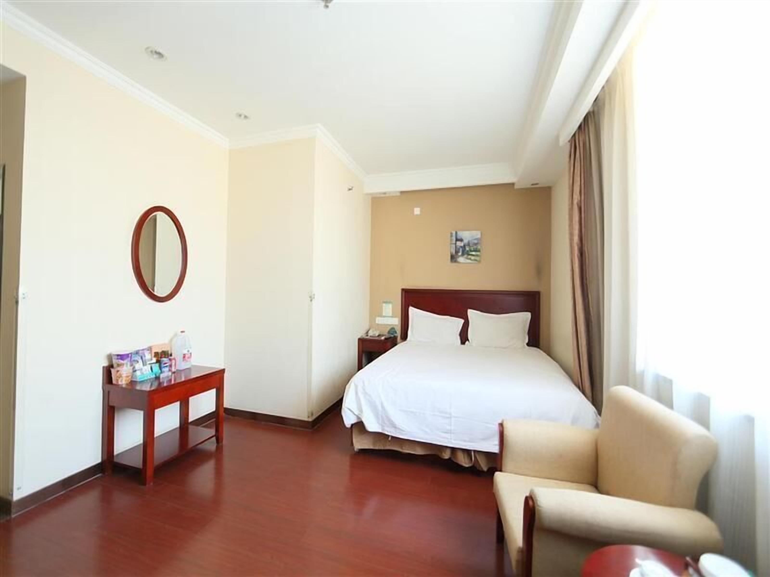 Quarto de hotel com uma cama, uma cadeira, uma escrivaninha, um espelho e um quadro na parede.