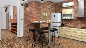 Uma cozinha moderna com parede de tijolos, banquetas, geladeira branca e piso de madeira.