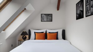 Quarto com cama grande, duas almofadas, mesa de cabeceira com abajur e uma obra de arte emoldurada na parede.