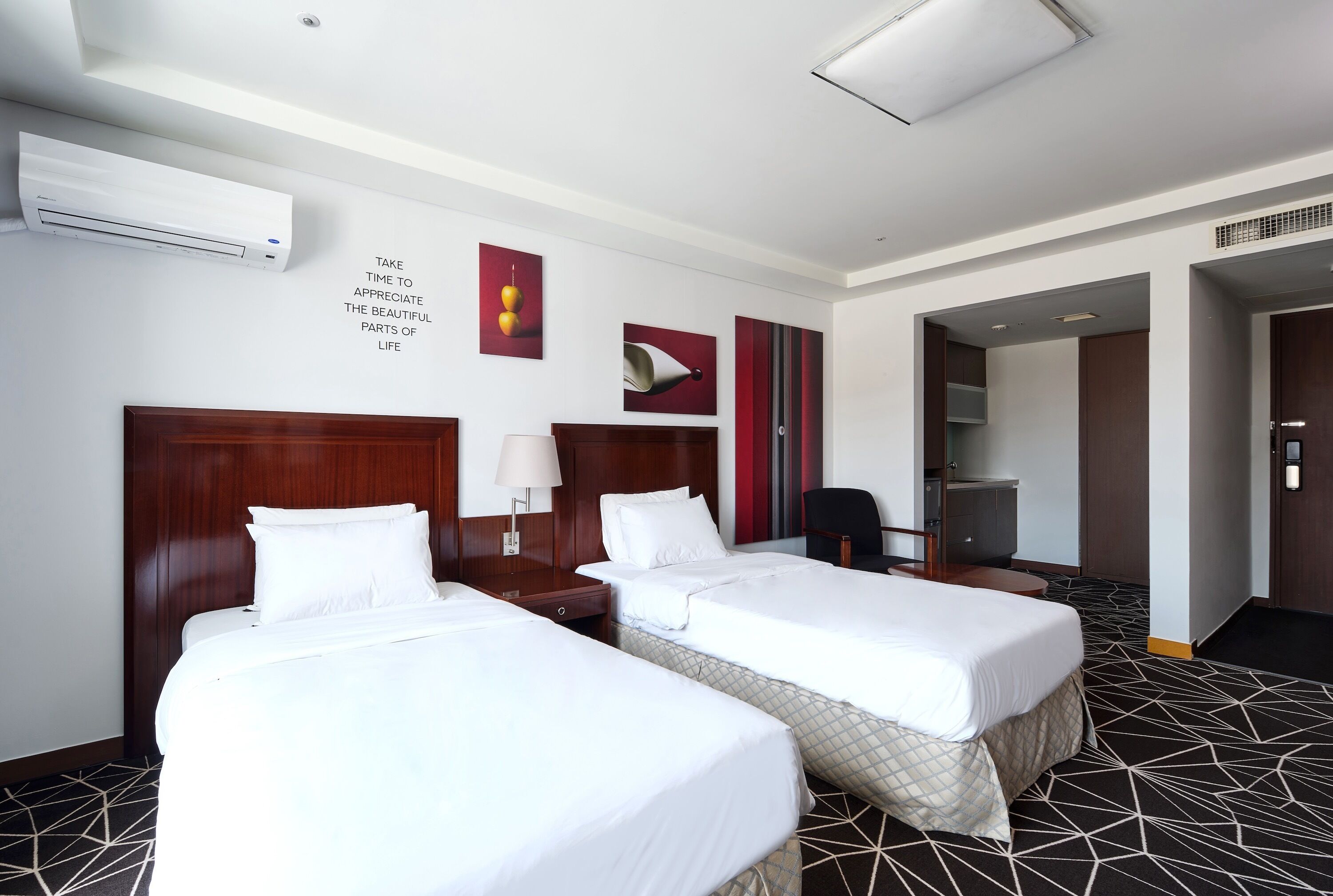 Quarto de hotel com duas camas, uma escrivaninha, uma cadeira, uma televisão e ar condicionado.