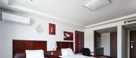 Quarto de hotel com duas camas, uma escrivaninha, uma cadeira, uma televisão e ar condicionado.